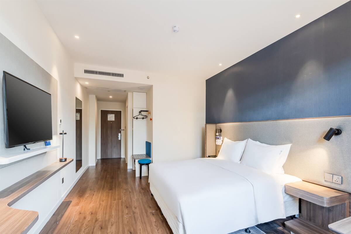 Quarto de hotel moderno com uma cama grande, televisão de tela plana e piso de madeira.