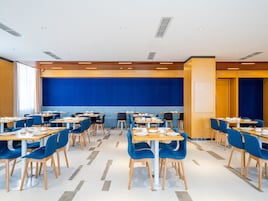 Uma sala de conferência com mesas, cadeiras, uma grande tela azul e painéis de madeira nas paredes.