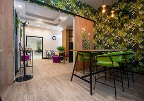 Um interior moderno com piso de madeira, cadeiras verdes, uma mesa de madeira e uma parede com padrão de folhas.