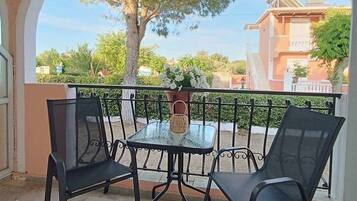 Uma varanda com mesa e cadeiras, um vaso de planta e vista para árvores e edifícios.