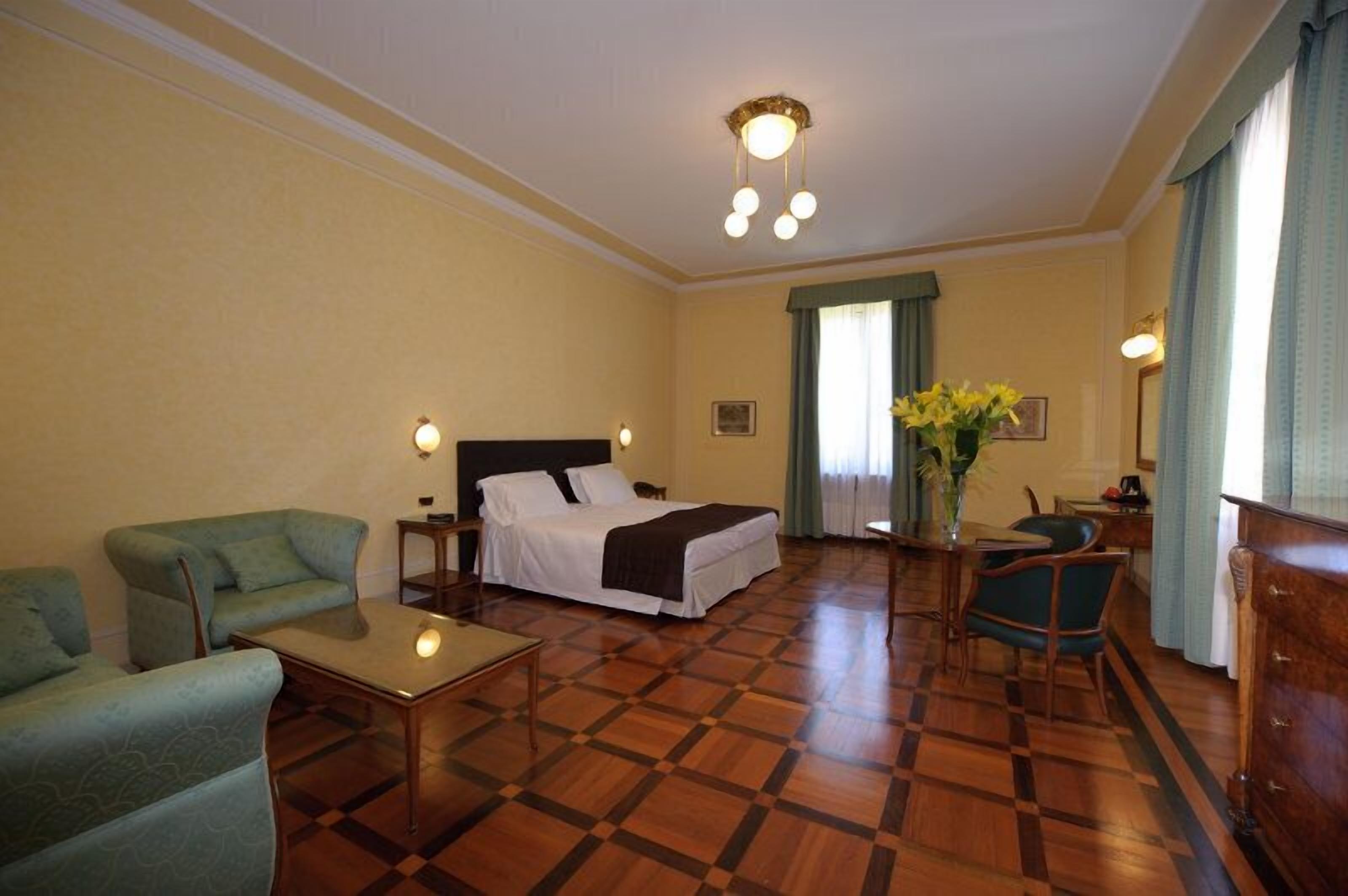 Quarto de hotel com uma cama, duas poltronas, uma mesa pequena, uma escrivaninha e um penteado.