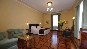 Quarto de hotel com uma cama, duas poltronas, uma mesa pequena, uma escrivaninha e um penteado.