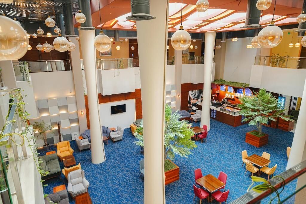 Um hall amplo com várias áreas de estar, um bar central e uma grande planta de interior.