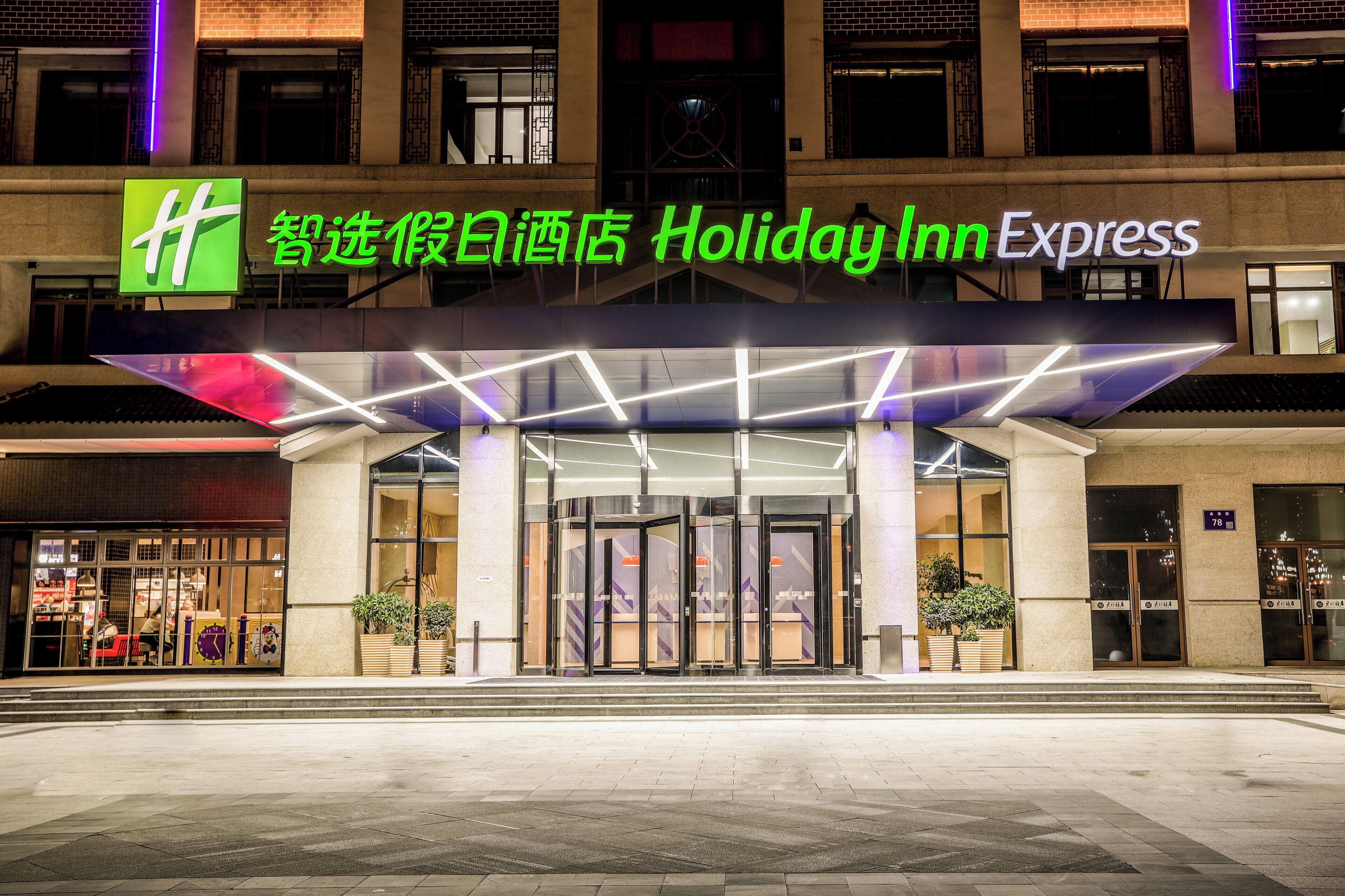 Entrada de um hotel Holiday Inn Express, com design moderno, apresentando um letreiro de neon chamativo e uma área de entrada coberta.