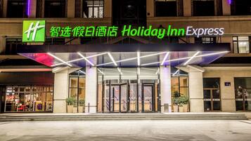 Entrada de um hotel Holiday Inn Express, com design moderno, apresentando um letreiro de neon chamativo e uma área de entrada coberta.