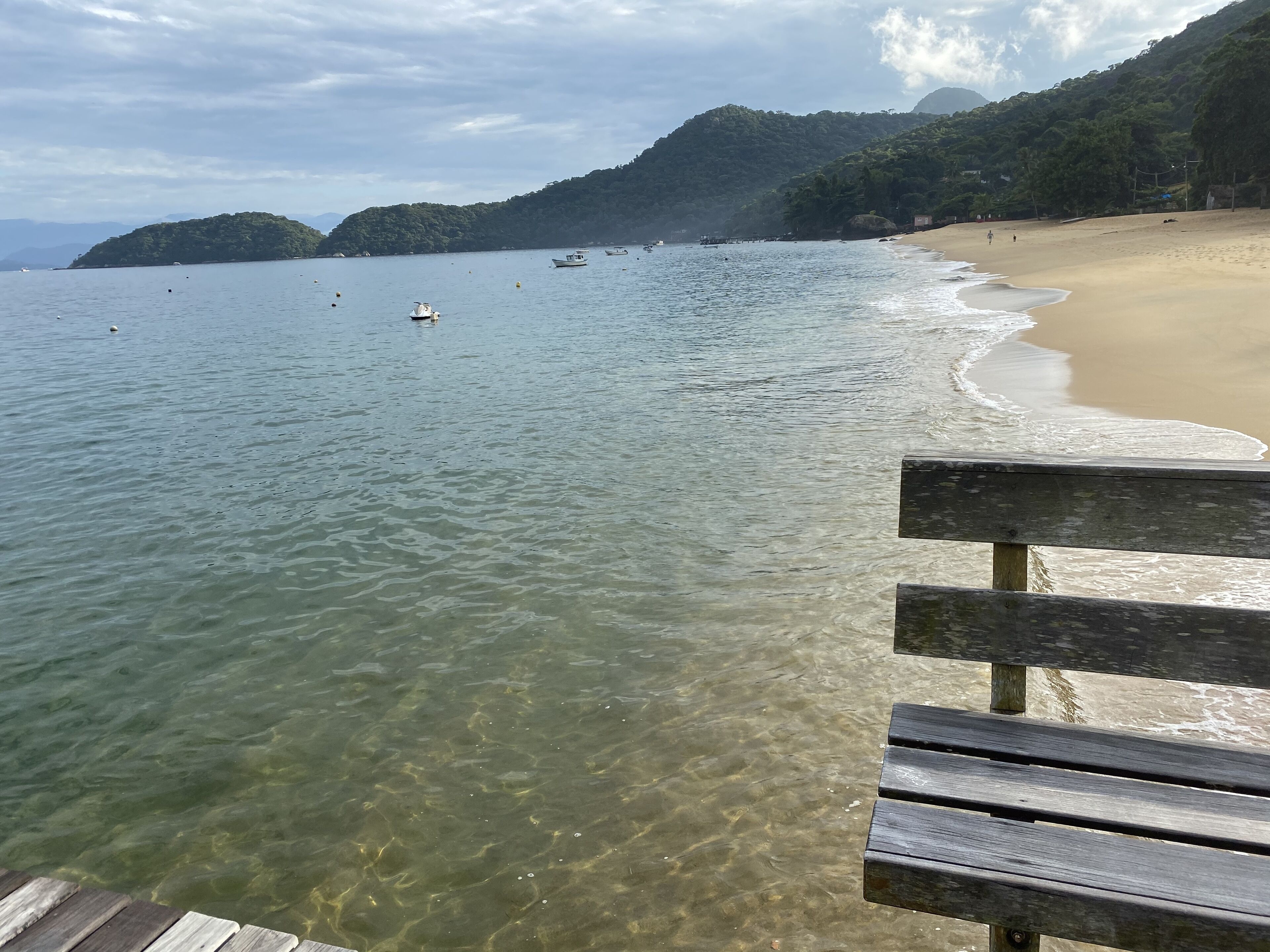 Um banco de madeira com vista para uma praia, água cristalina e barcos.