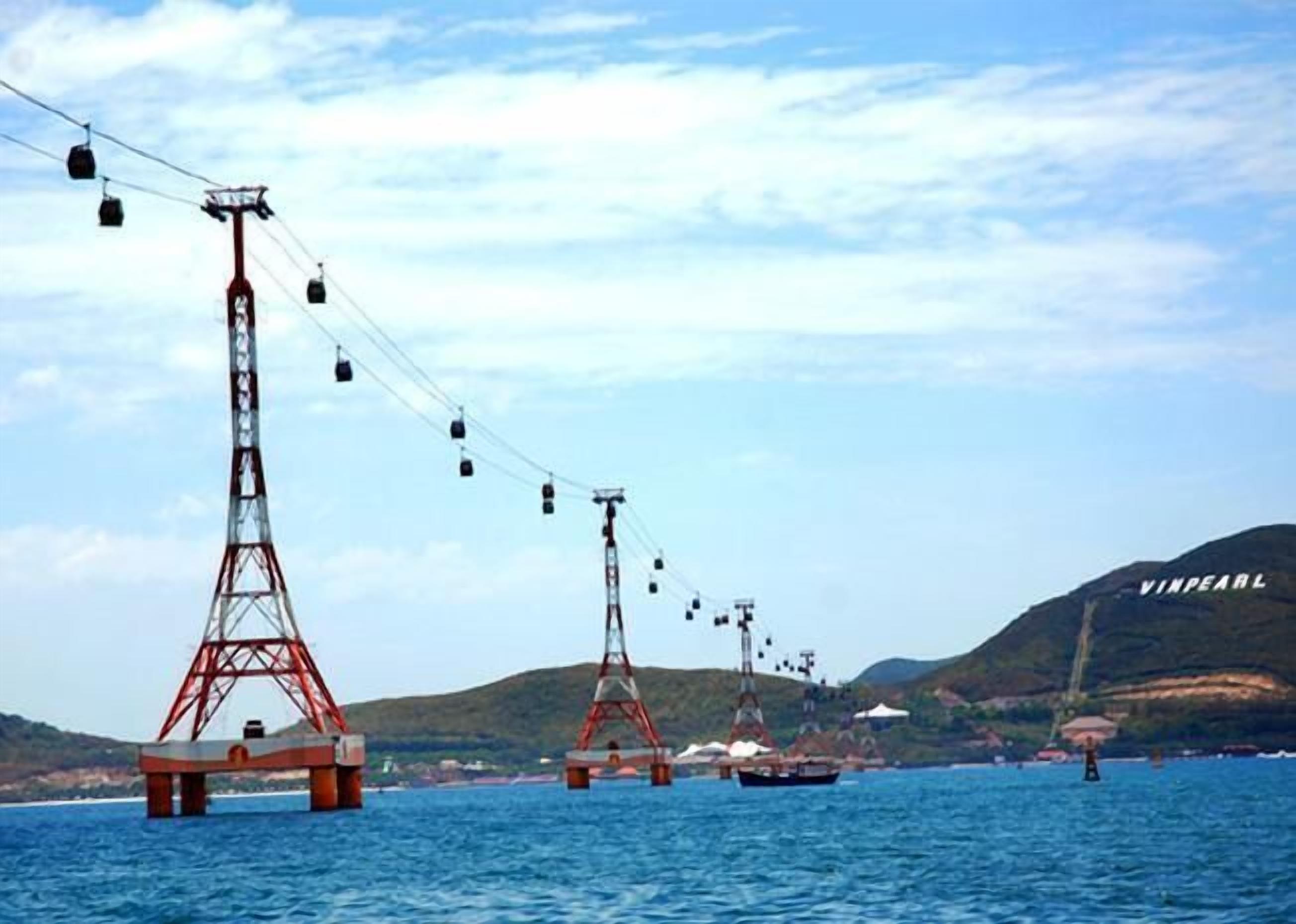 Vários teleféricos sobre a água, com montanhas ao fundo e a inscrição 'VINPEARL' visível numa colina.