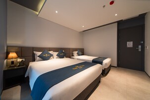 Quarto de hotel com duas camas, uma mesa de cabeceira, um abajur e uma porta.
