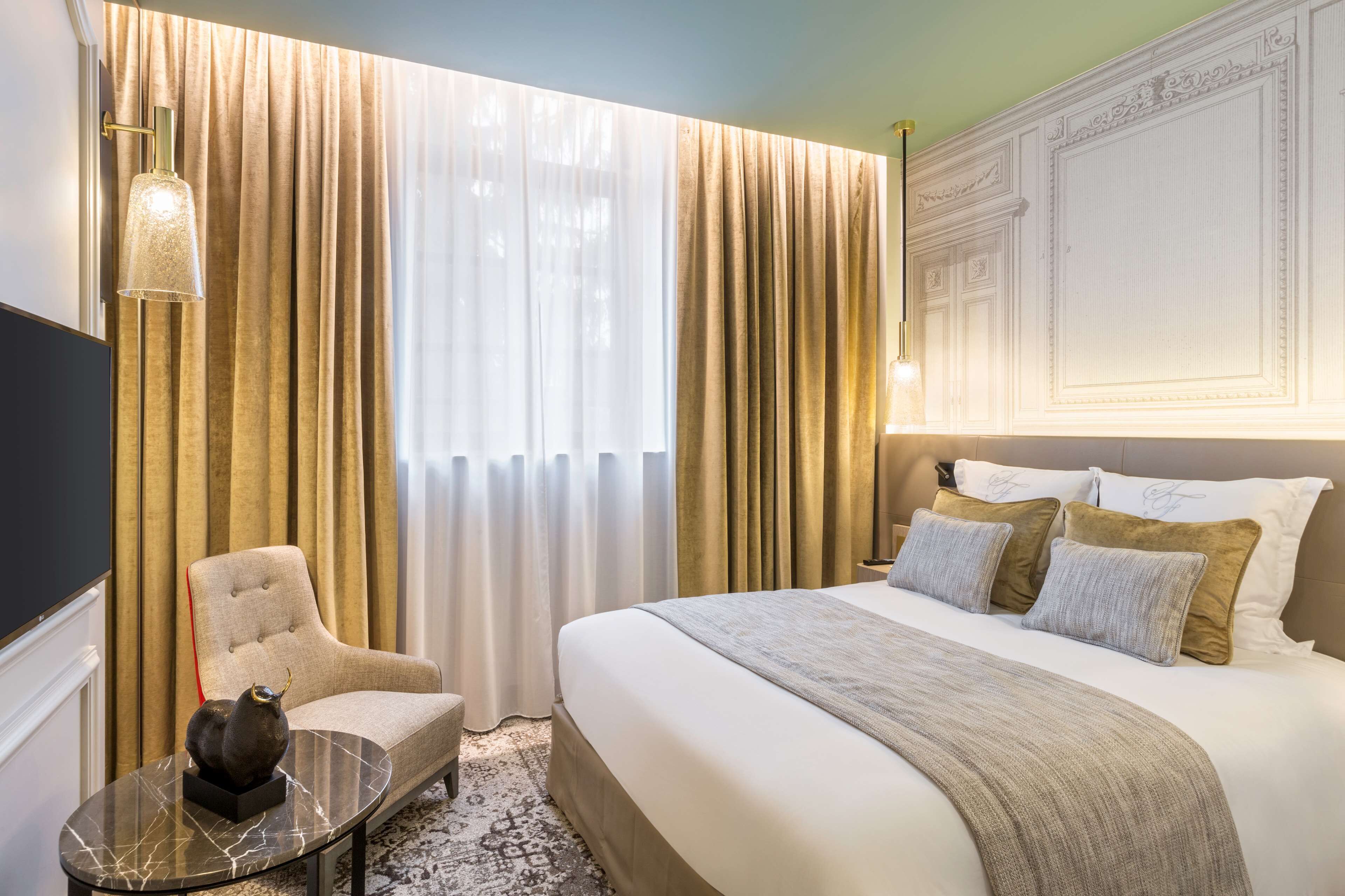 Quarto de hotel com uma cama grande, uma cadeira, uma mesinha e uma televisão.