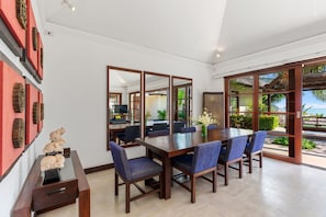 Uma área de refeições com uma mesa de madeira e cadeiras azuis, uma escultura decorativa e uma janela grande com vista para vegetação e um edifício.