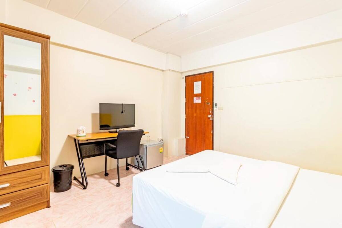 Quarto de hotel com cama, escrivaninha com cadeira, televisão, guarda-roupa e porta.