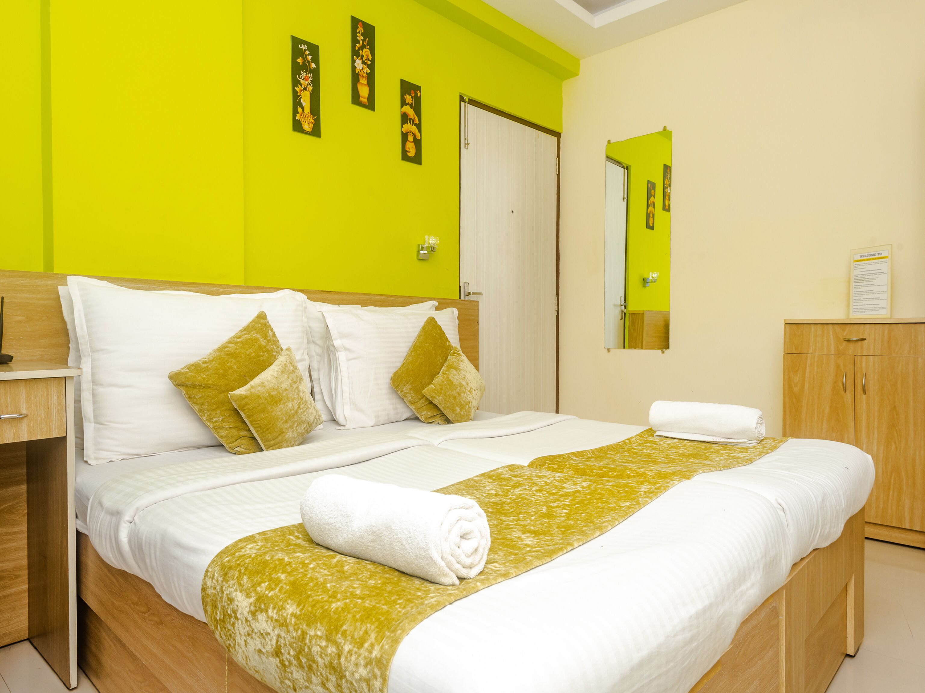Quarto de hotel com cama, almofadas, mesa de cabeceira, guarda-roupa e espelho.