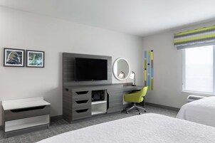 Quarto de hotel moderno com uma cama grande, uma escrivaninha com TV de tela plana, uma cadeira e uma janela com vista.