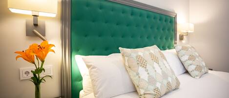 Quarto de hotel com cabeceira estofada verde, roupa de cama branca e almofadas estampadas.