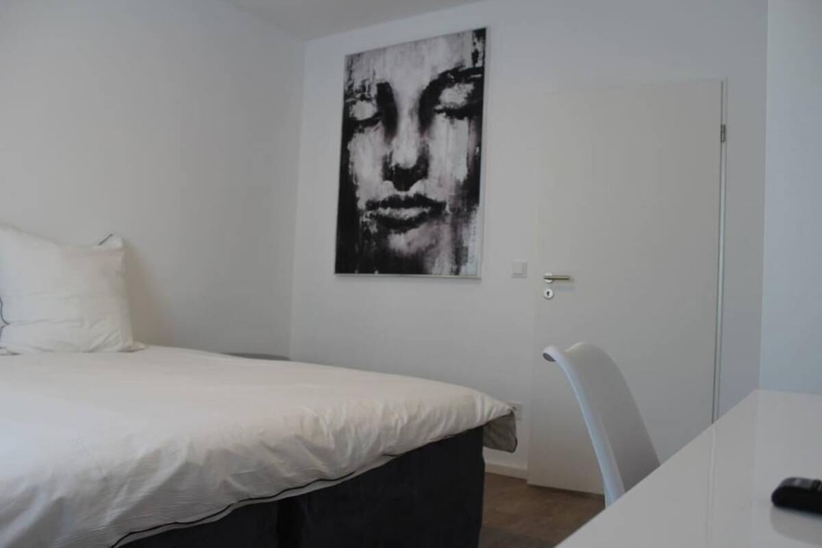 Quarto com cama, uma cadeira, uma mesa e uma porta.