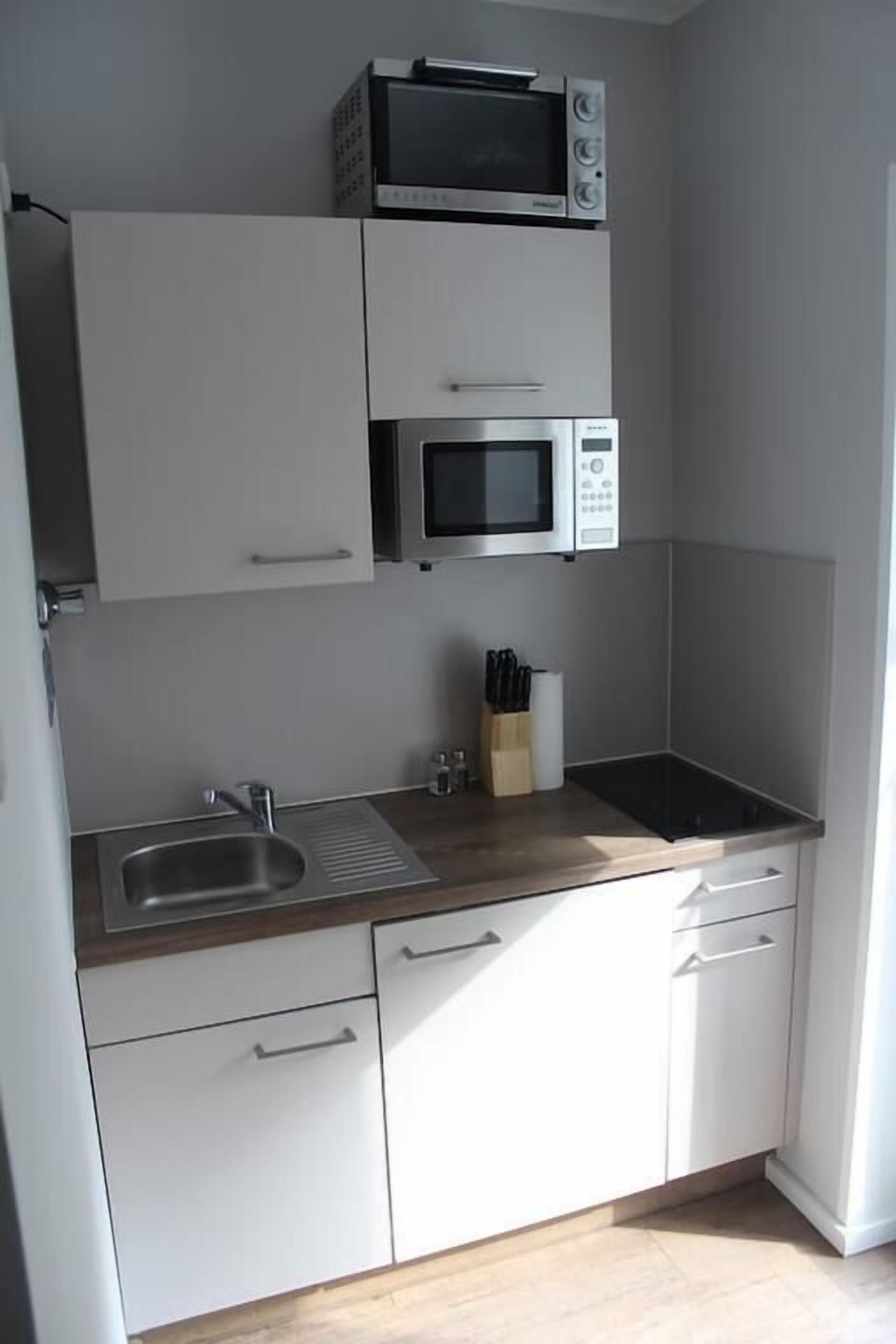 Cozinha compacta com armários brancos, pia de aço inoxidável, micro-ondas e porta-facas.