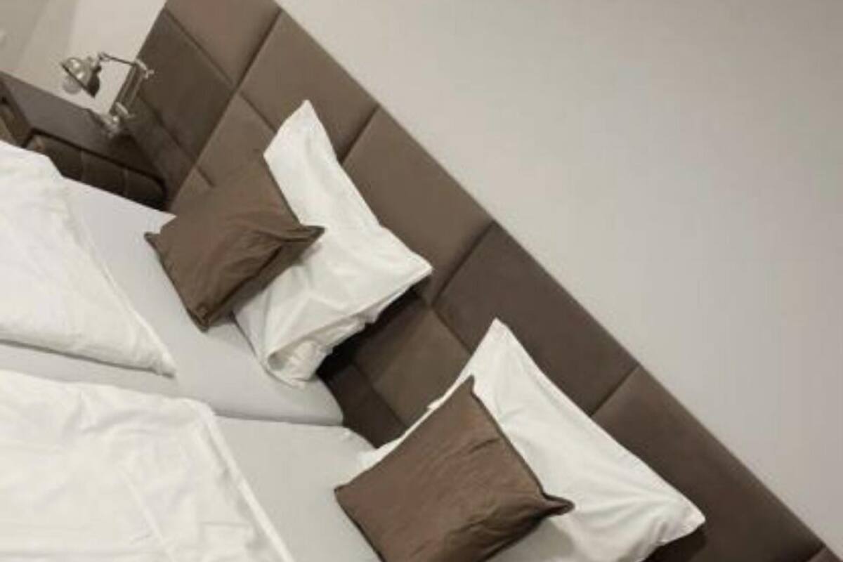 Quarto de hotel com uma cama grande, duas almofadas, uma mesa de cabeceira e uma luminária.