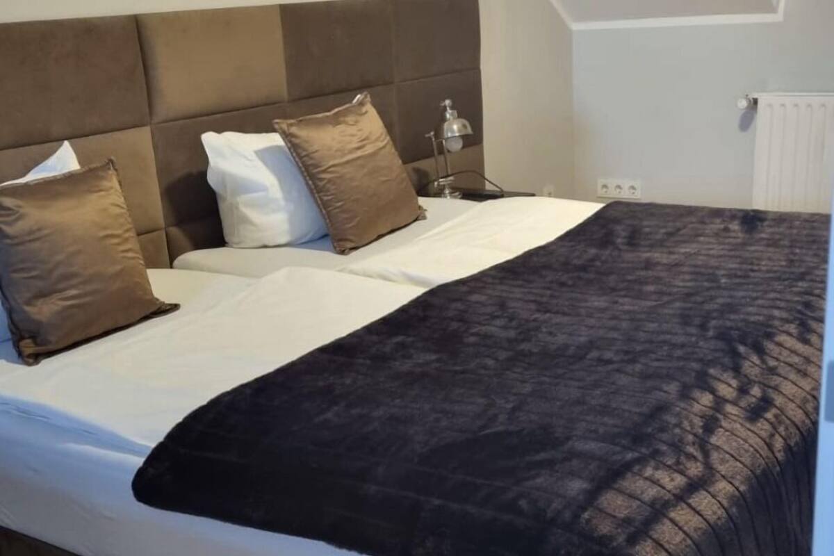 Quarto com teto inclinado, uma cama com cabeceira escura e uma janela.