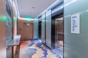 Corredor de hotel com elevador, placa de indicação e carpete estampado.