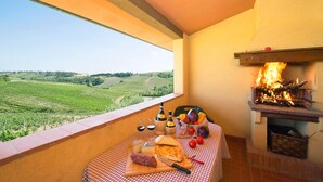 Uma varanda com uma mesa posta para refeição, lareira e vista para um vinhedo.