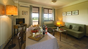 Quarto mobiliado com mesa de jantar posta para refeição, sofá, televisão e janela com cortinas.
