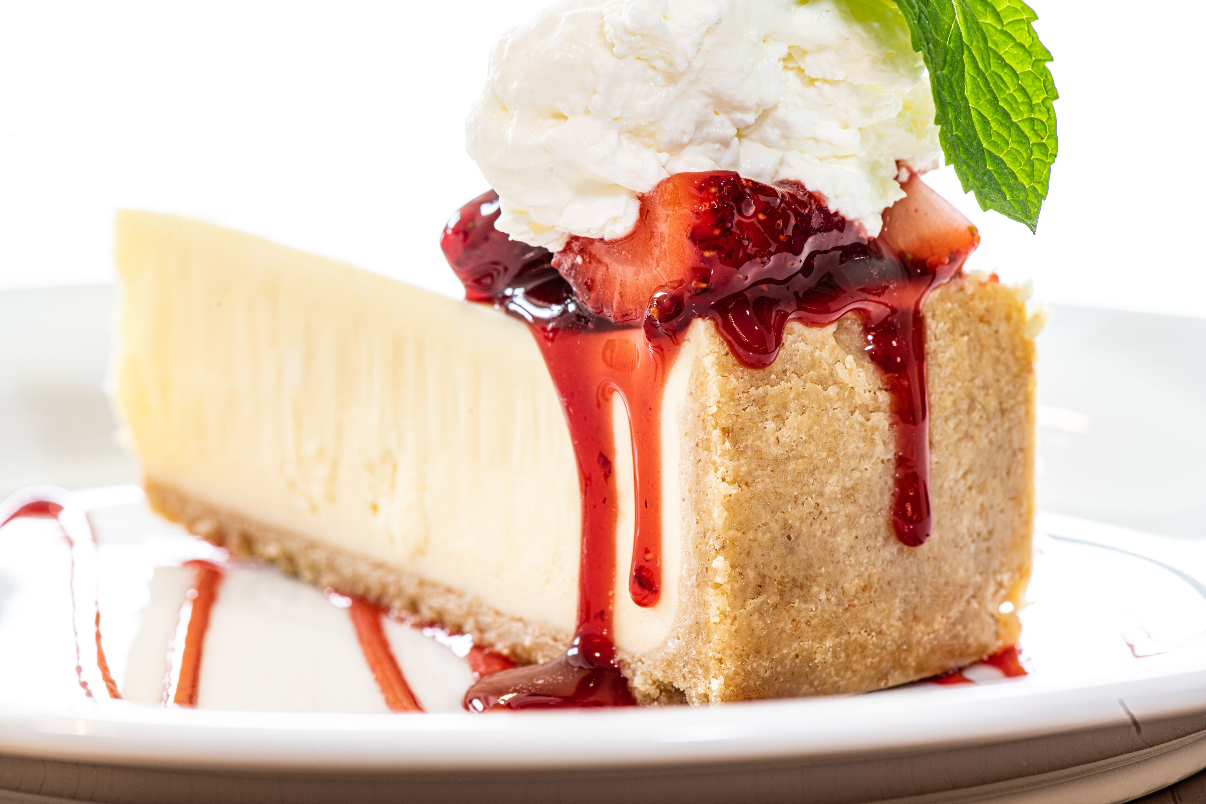 Uma fatia de cheesecake com compota de frutas vermelhas e chantilly sobre um prato branco.