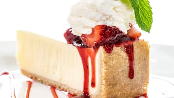 Uma fatia de cheesecake com compota de frutas vermelhas e chantilly sobre um prato branco.