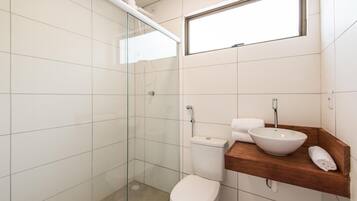 Uma casa de banho moderna com chuveiro envidraçado, sanita branca e toucador de madeira com lavatório.