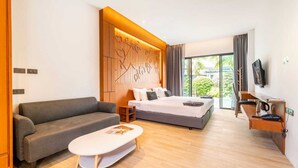 Quarto de hotel moderno com cama, sofá, mesa de centro e televisão.