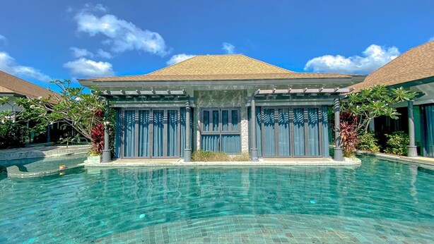 Um resort moderno com piscina cristalina, edifícios de dois andares com grandes janelas e paisagismo tropical.