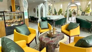 Um hall amplo com cadeiras amarelas, uma mesa redonda central e uma vitrine com doces.
