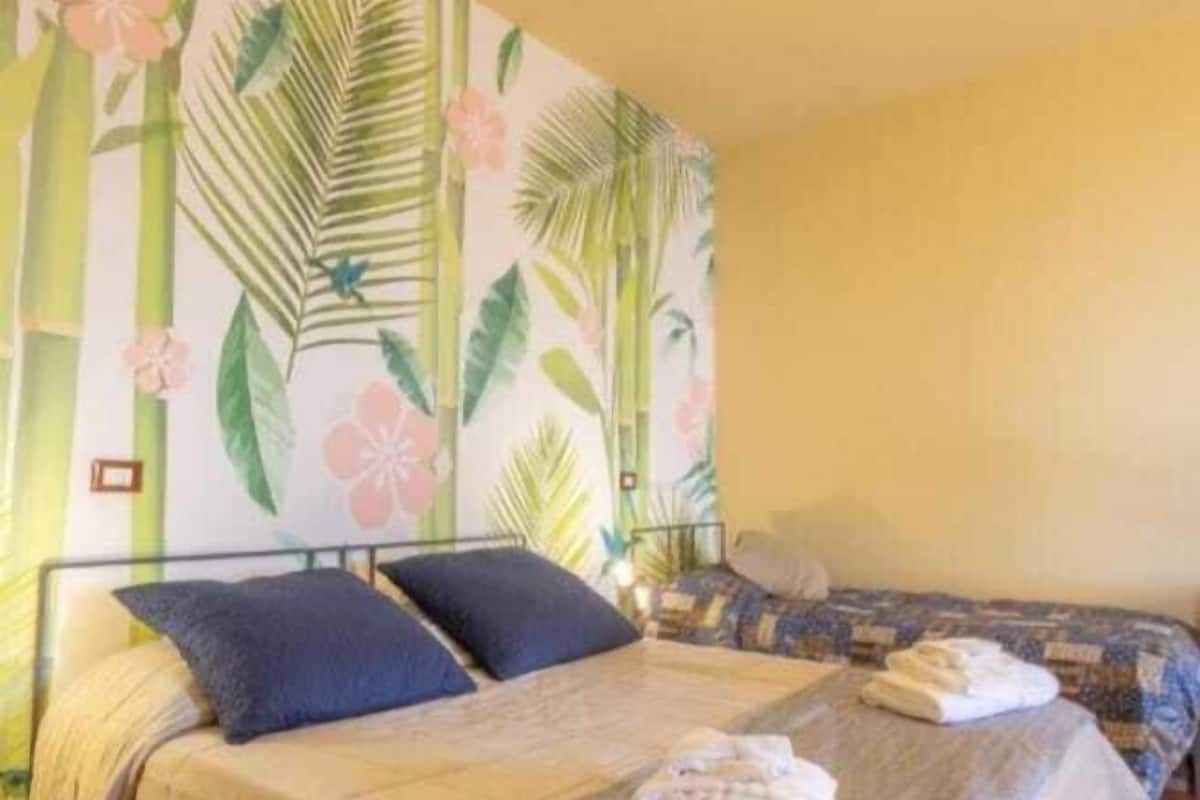 Quarto com cama, duas almofadas, toalha dobrada e parede com padrão floral e de bambu.