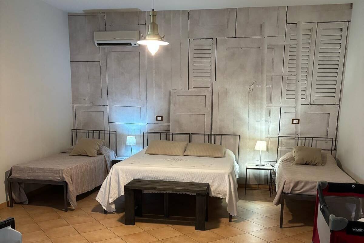 Quarto com duas camas, um banco, uma escrivaninha e um carrinho.