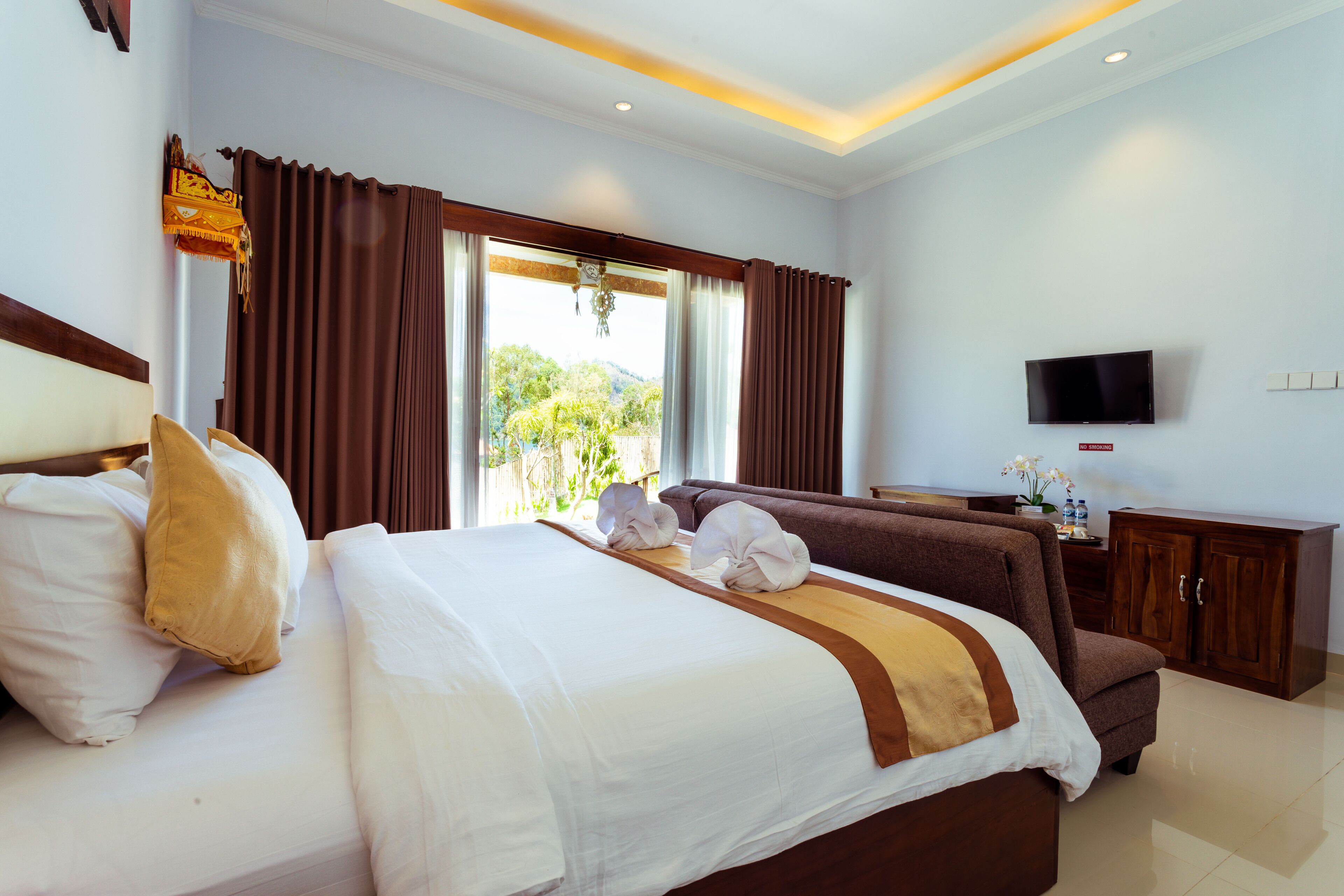 Quarto de hotel com cama grande, sofá, TV e vista para o exterior.