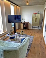 Uma sala de estar moderna com televisão de tela plana, sofá, mesa de centro, escrivaninha e uma cadeira.