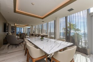 Uma sala de estar ampla com uma grande mesa de mármore, assentos confortáveis e vista para o oceano.