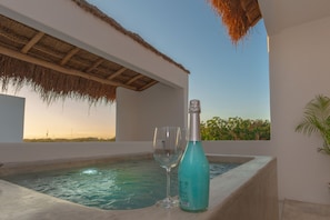 Uma área de piscina com garrafa e copo, um telhado de palha e vista para o verde.
