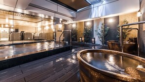 Uma área de spa moderna com banheira de hidromassagem, piso de madeira e parede de vidro refletindo o interior.