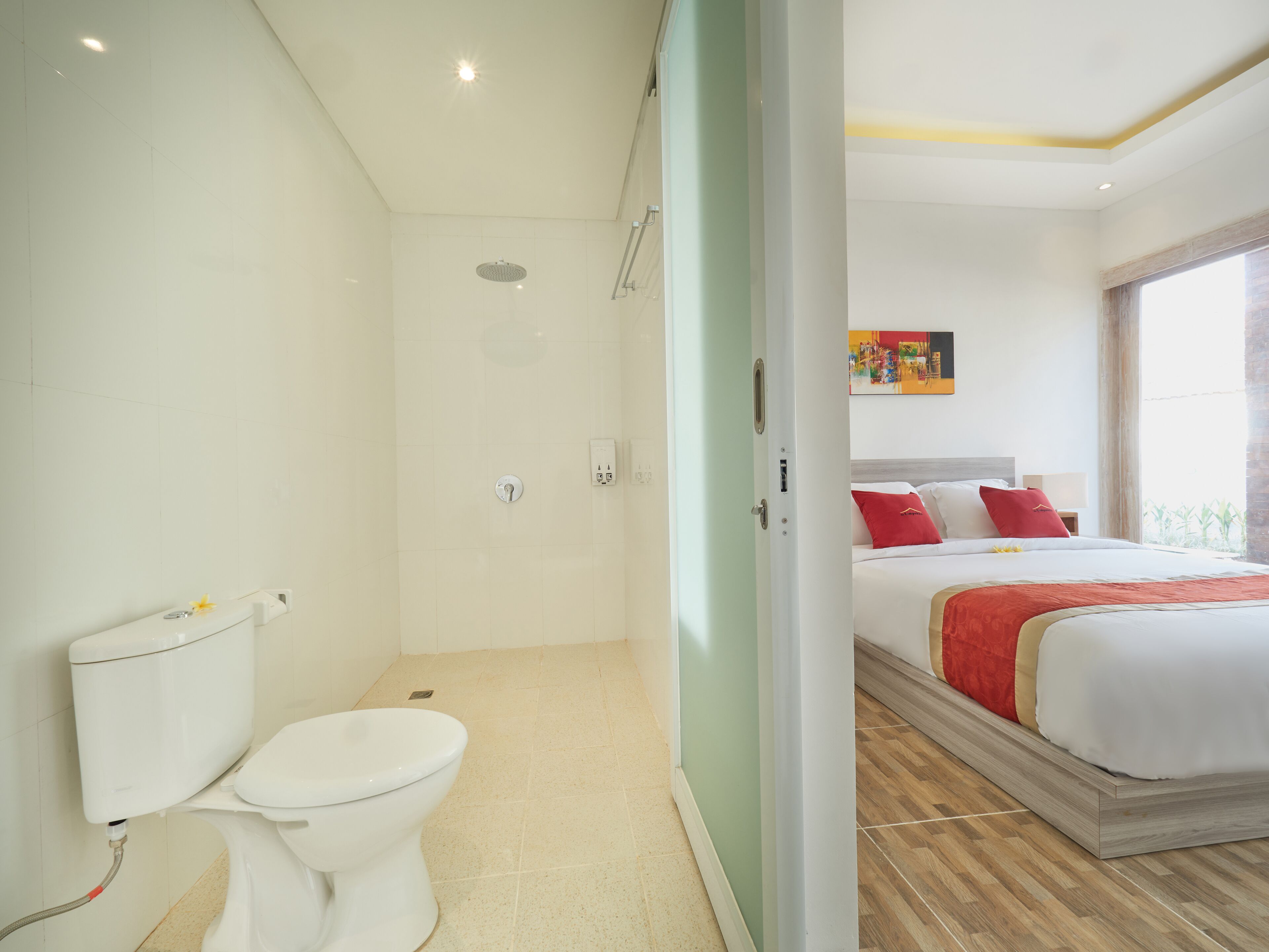 Quarto de hotel com sanita, chuveiro e cama com almofadas vermelhas.