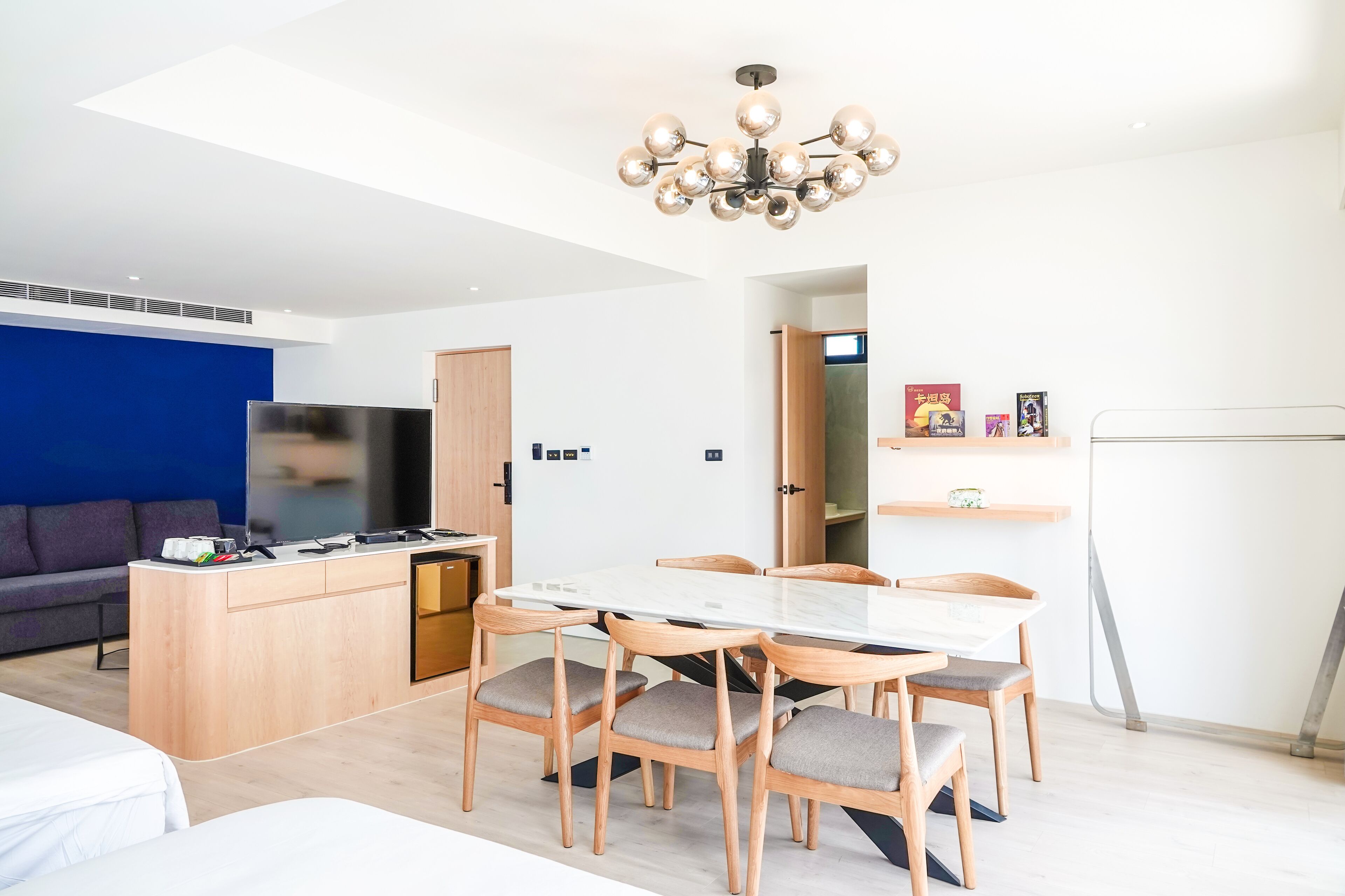 Uma cozinha moderna com uma ilha central, uma área de refeições com mesa e cadeiras brancas, e uma sala de estar com sofá e televisão.