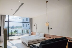 Quarto de hotel moderno com uma cama grande, um sofá, uma varanda vista para o mar e uma janela ampla.
