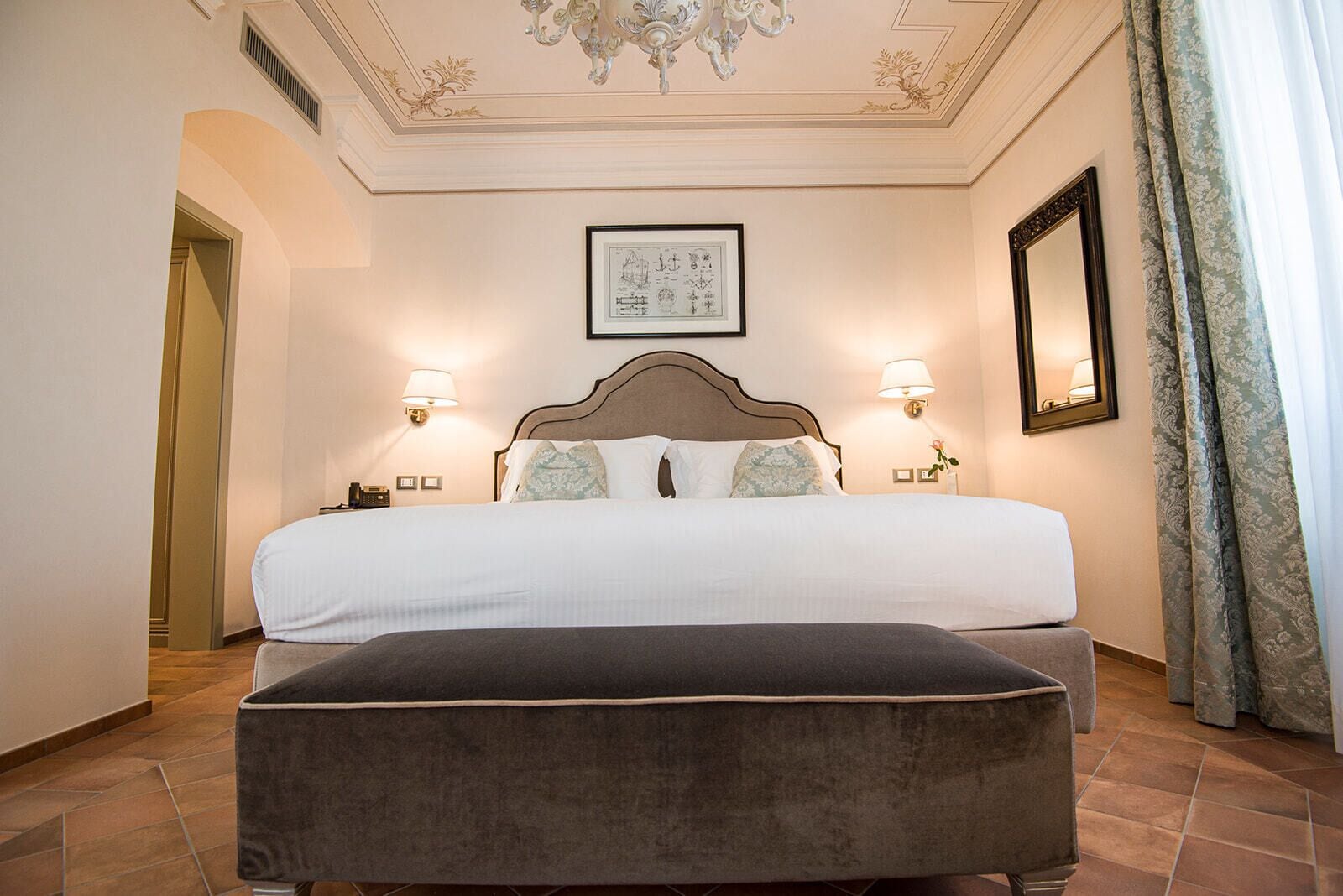 Quarto de hotel com uma cama grande, duas luminárias de cabeceira, um quadro na parede e um candelabro.