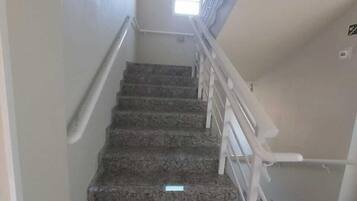 Uma escadaria com degraus de granito, corrimãos brancos e uma pequena janela no topo.