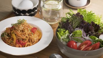 Uma mesa de jantar com um prato de massa, uma salada, uma chávena de café e um copo de água.