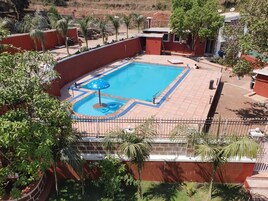 Piscina cercada por um muro vermelho, com palmeiras e uma grade.