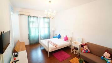 Quarto com cama, sofá, televisão, escrivaninha e janela com cortinas.