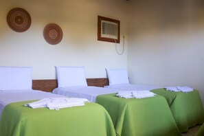Quarto de hotel com duas camas de solteiro, cada uma com colchas verdes e almofadas brancas, e uma pequena mesa com toalhas dobradas.