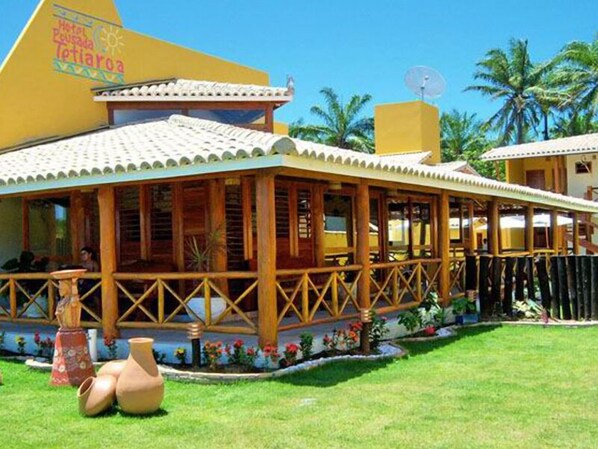 Um hotel com design tradicional, apresentando um pátio coberto com grades de madeira e um pequeno jardim com vasos de plantas e objetos decorativos.