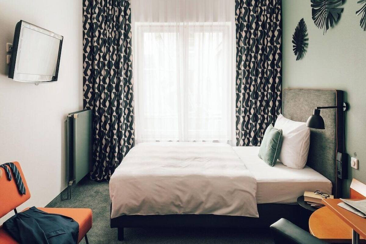 Quarto de hotel com cama, escrivaninha, cadeira e televisão.