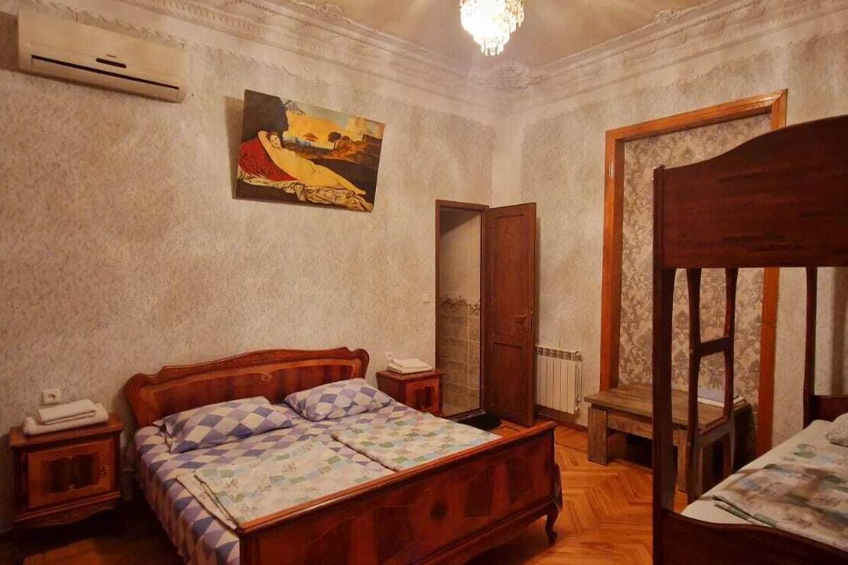 Quarto com duas camas de madeira, uma mesinha de cabeceira, cômoda e um quadro na parede, além de um lustre.